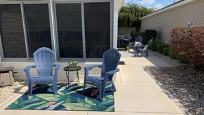 Um pátio com duas cadeiras Adirondack, uma mesinha e uma planta decorativa.