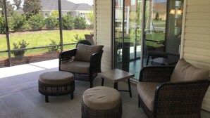 Varanda coberta com mobiliário de vime, porta de vidro que dá para o exterior e vista para uma área residencial.