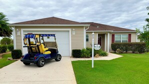 Uma casa residencial com garagem, gramado e um carrinho de golfe estacionado na frente.
