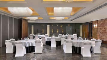 Uma sala de banquetes com mesas redondas, cadeiras brancas e lustres.