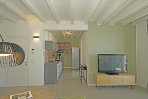 Uma cozinha moderna com ilha central, área de refeições com mesa e sala de estar com televisão e armário de madeira.