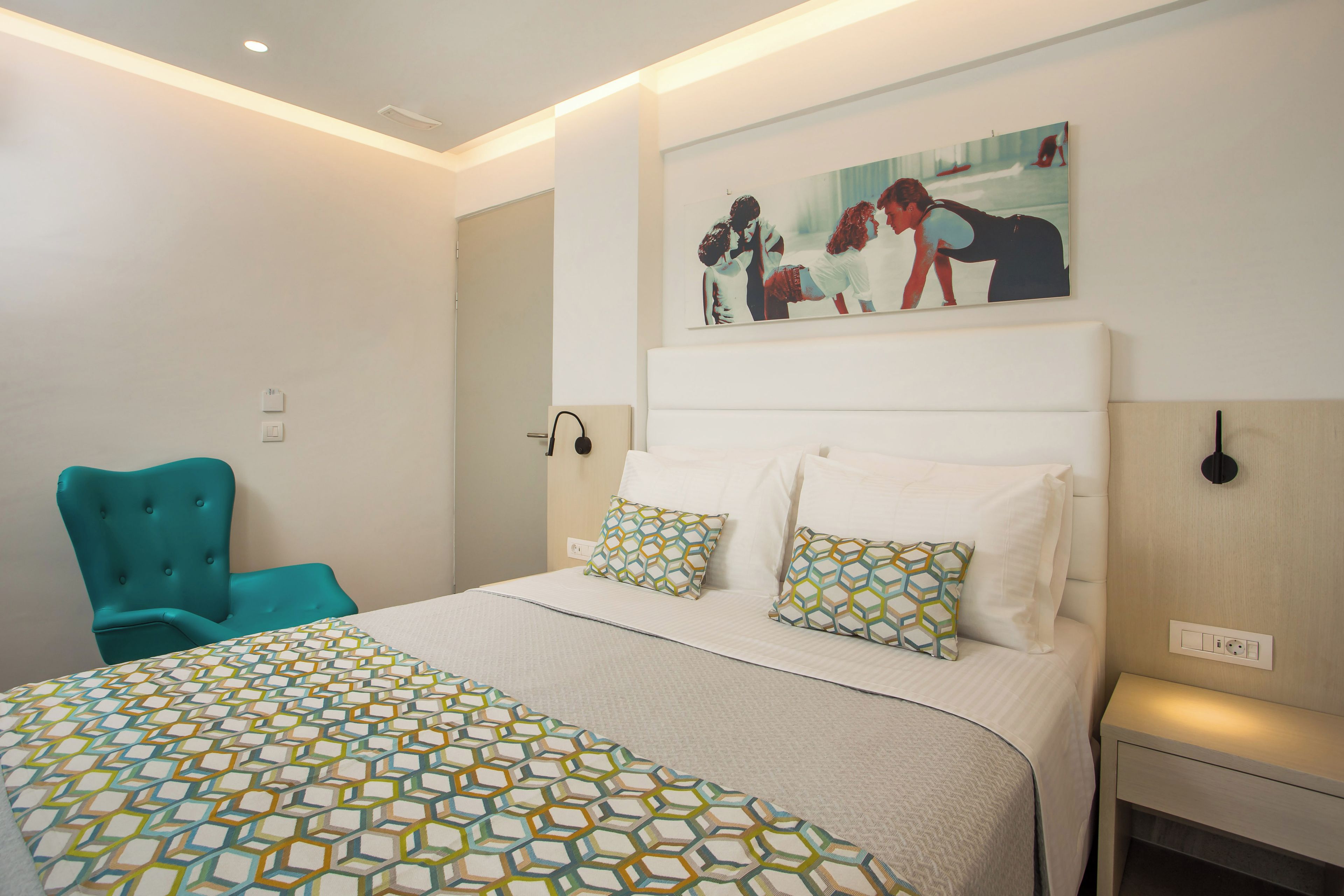 Um quarto com cama, poltrona, quadro e mesa de cabeceira.