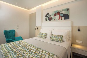 Um quarto com cama, poltrona, quadro e mesa de cabeceira.