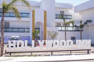 Um edifício moderno com um grande letreiro 'HOLLYWOOD INN', palmeiras e um carro estacionado.