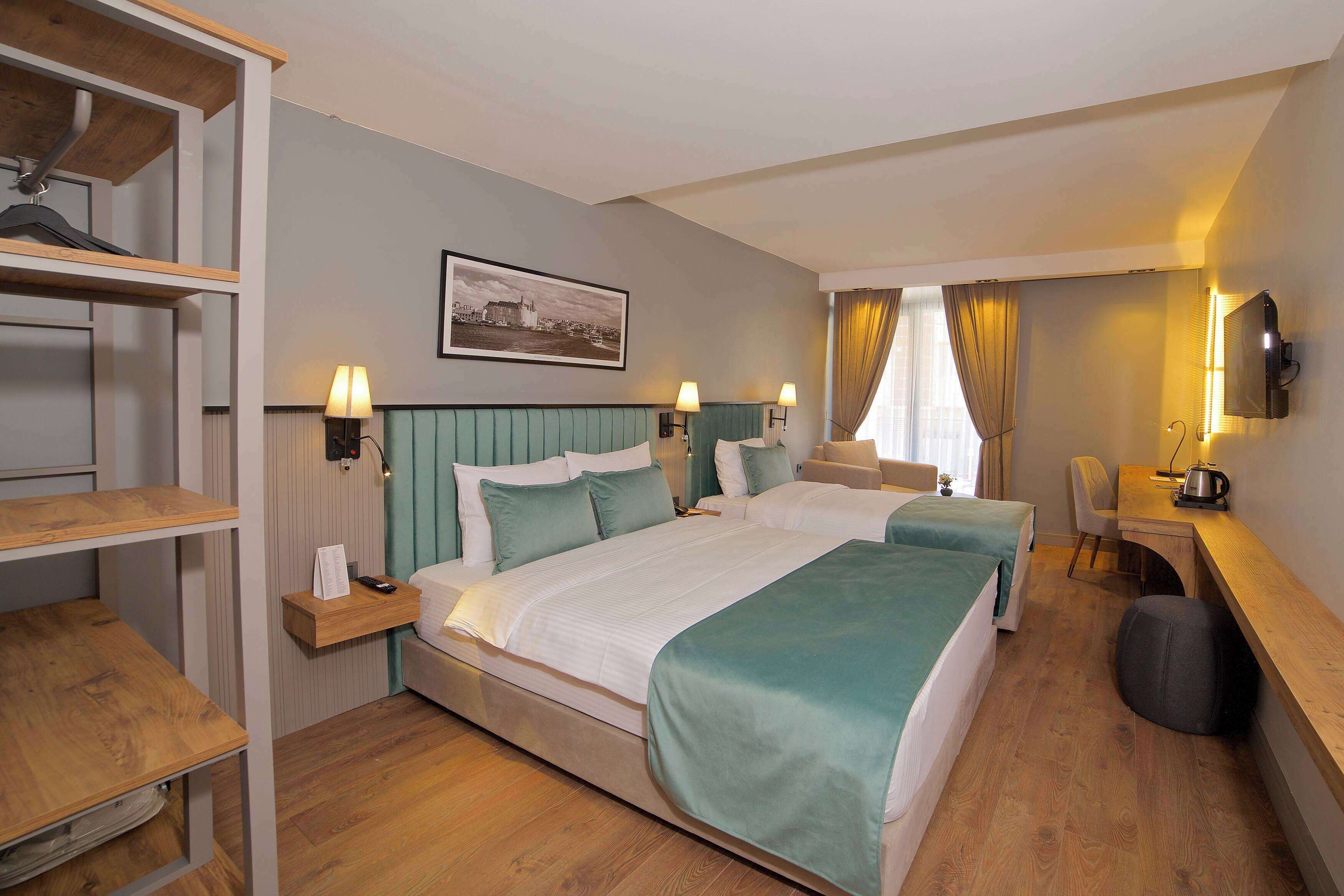Quarto de hotel com duas camas, uma escrivaninha, uma cadeira, uma televisão e um cabideiro.