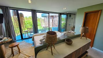 Quarto moderno com uma grande porta de vidro deslizante que dá para uma varanda, uma cama com lençóis brancos, um pequeno banquinho de madeira e duas cestas trançadas em um console.