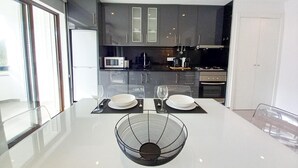 Cozinha moderna com armários escuros, micro-ondas e área de jantar com mesa e cadeiras de vidro.