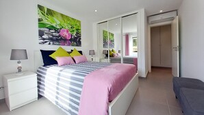 Quarto moderno com uma cama grande, mesas de cabeceira, um guarda-roupa e um espelho.
