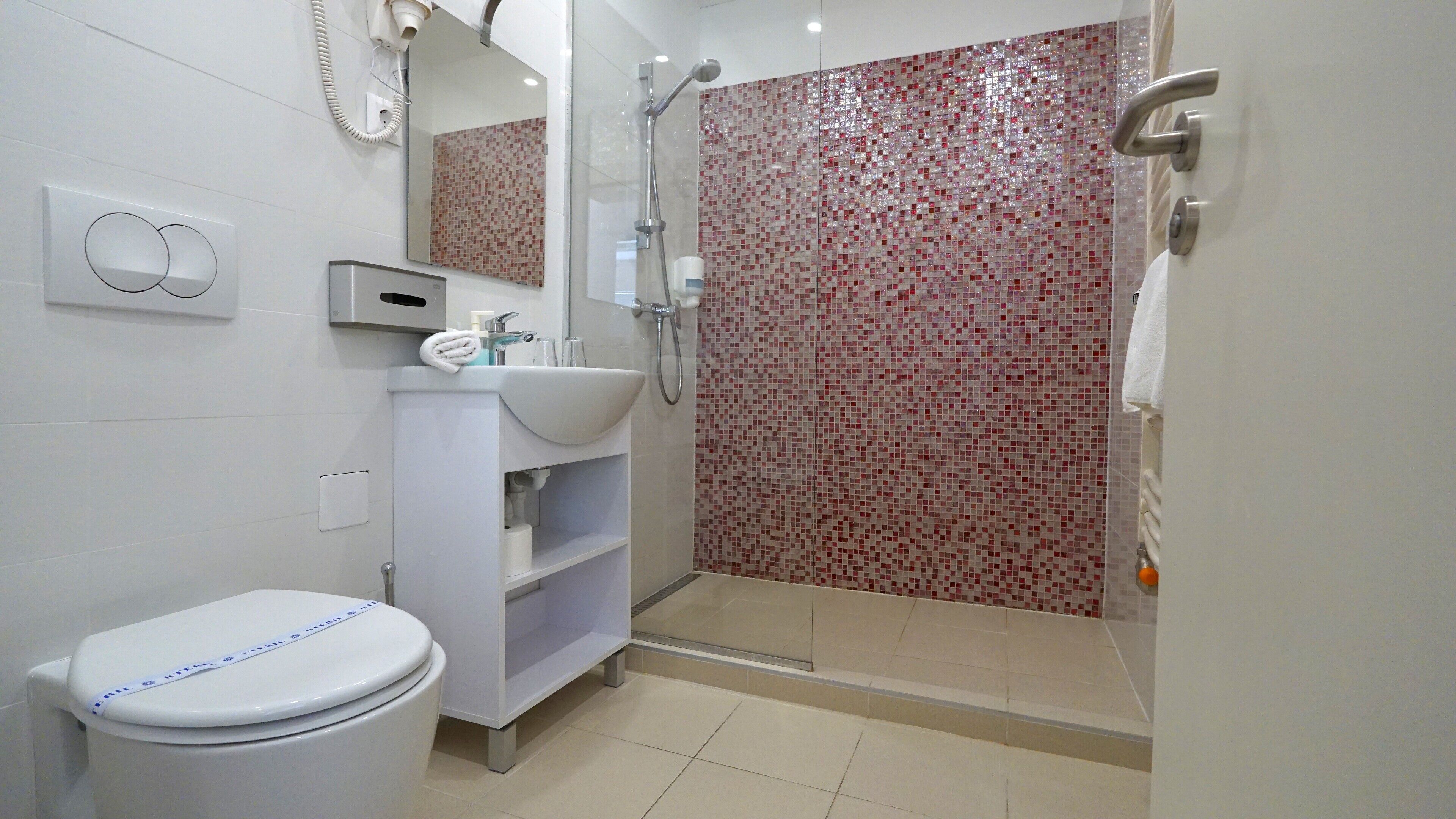 Uma casa de banho moderna com sanita branca, lavatório e chuveiro com parede de mosaico.