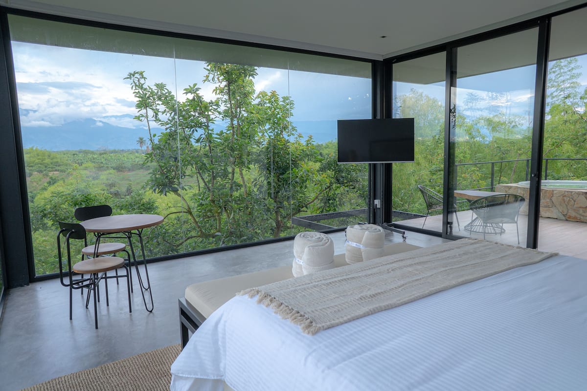 Quarto com cama grande, televisão e varanda com vista para a paisagem.