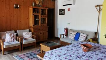 Um quarto aconchegante e rústico com móveis de madeira, uma cama grande com colcha florida, um armário de madeira e um ventilador de teto.