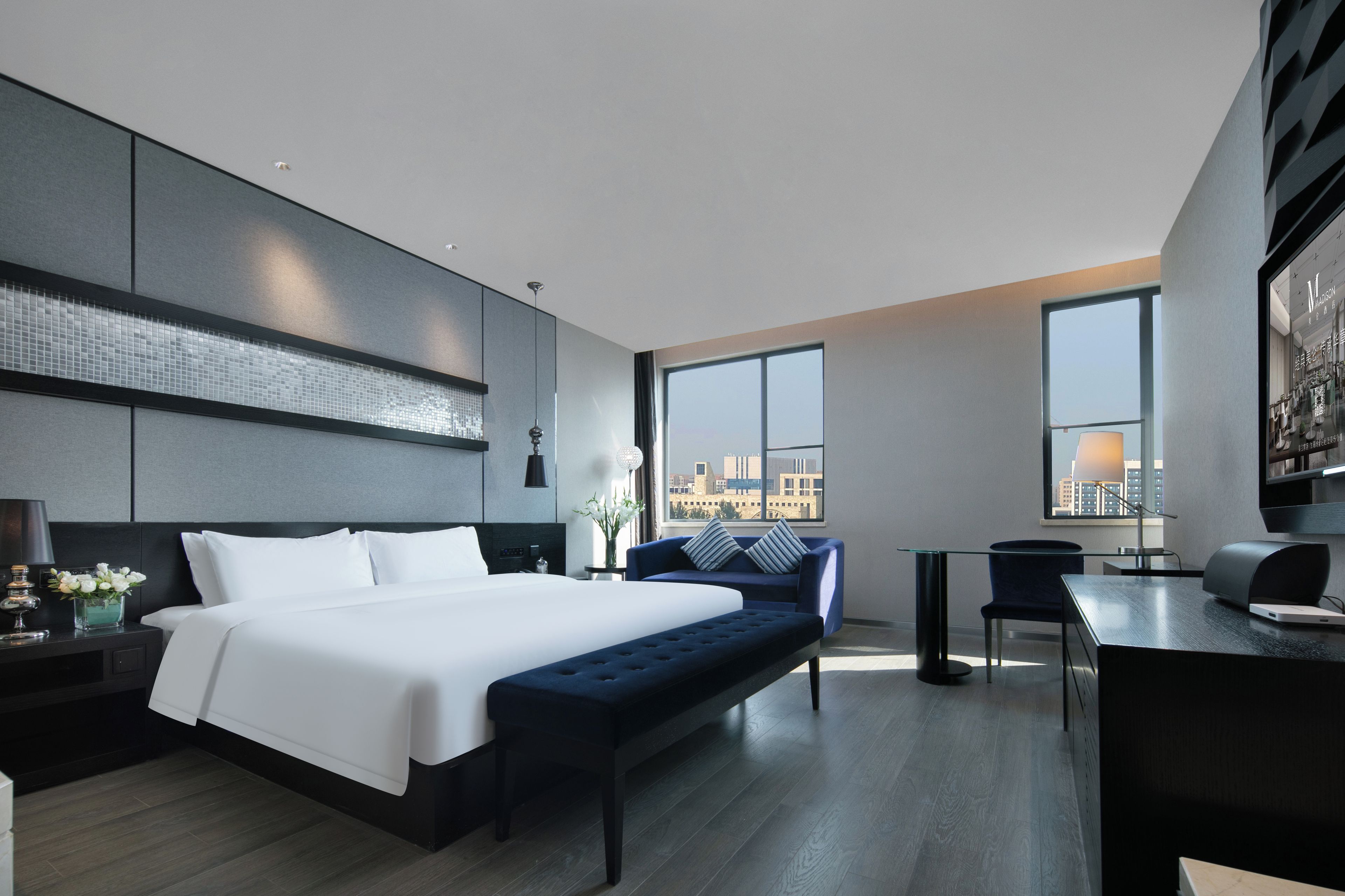 Quarto de hotel moderno com uma cama grande, área de estar, escrivaninha e vista para a cidade.