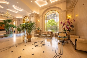 Um hall amplo com um candelabro, área de estar, plantas em vasos e uma grande janela com vista.