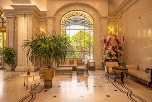 Um hall espaçoso com uma grande janela em arco, um sofá, cadeiras, uma mesa de centro e plantas em vasos.