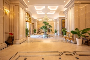 Um hall imponente com piso de mármore, um lustre central e painéis de parede simétricos.