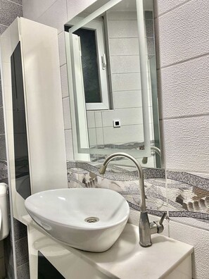 Casa de banho com lavatório branco, espelho e área de duche.