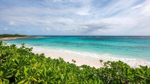 Uma praia com águas turquesa cristalinas e areia branca, cercada por vegetação verde exuberante.