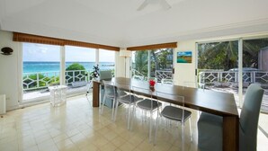 Uma zona de refeições com vista para o oceano, um ventilador de teto e uma mesa com cadeiras.