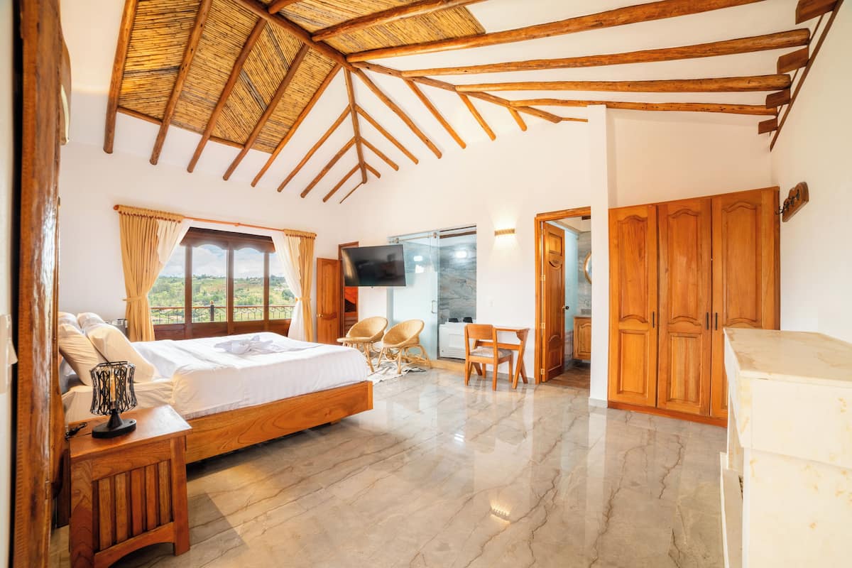 Quarto com cama, móveis de madeira, televisão e vista pela janela.