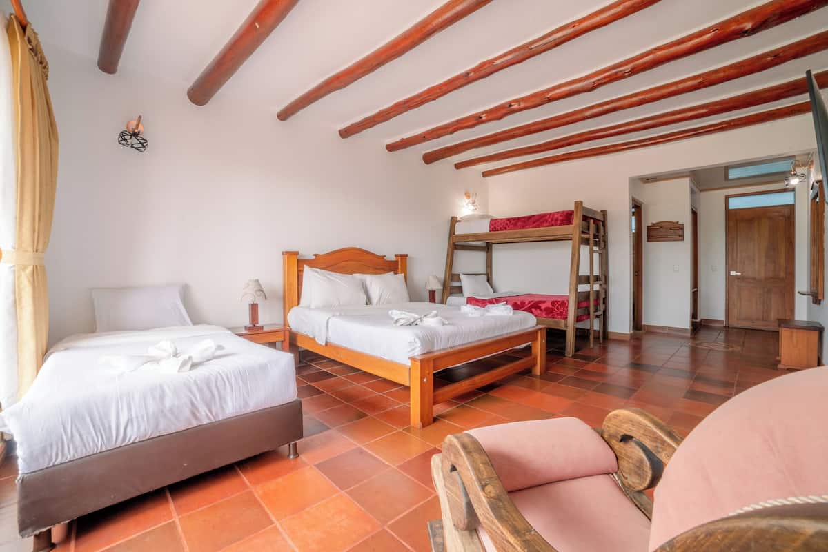 Quarto com duas camas, vigas de madeira, uma cama beliche e uma cadeira.