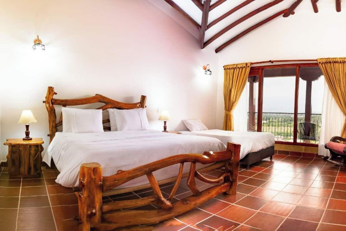 Quarto com cama grande, duas mesas de cabeceira, uma cadeira e varanda com cortinas.