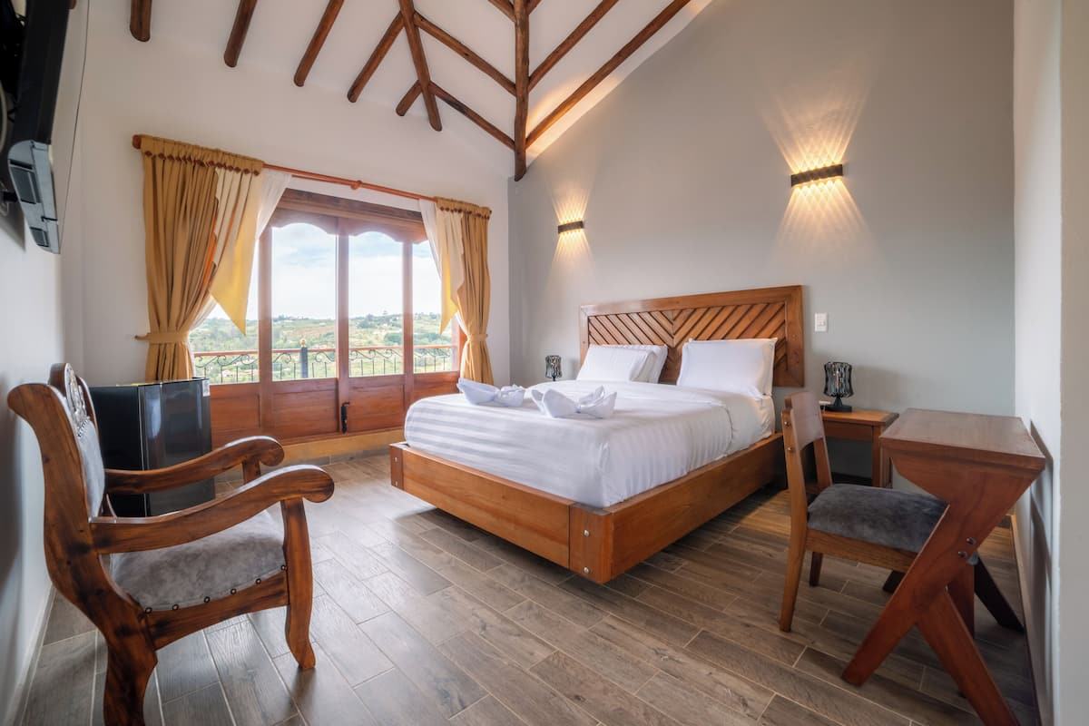 Quarto com cama de madeira, escrivaninha, cadeira e vista para o exterior.
