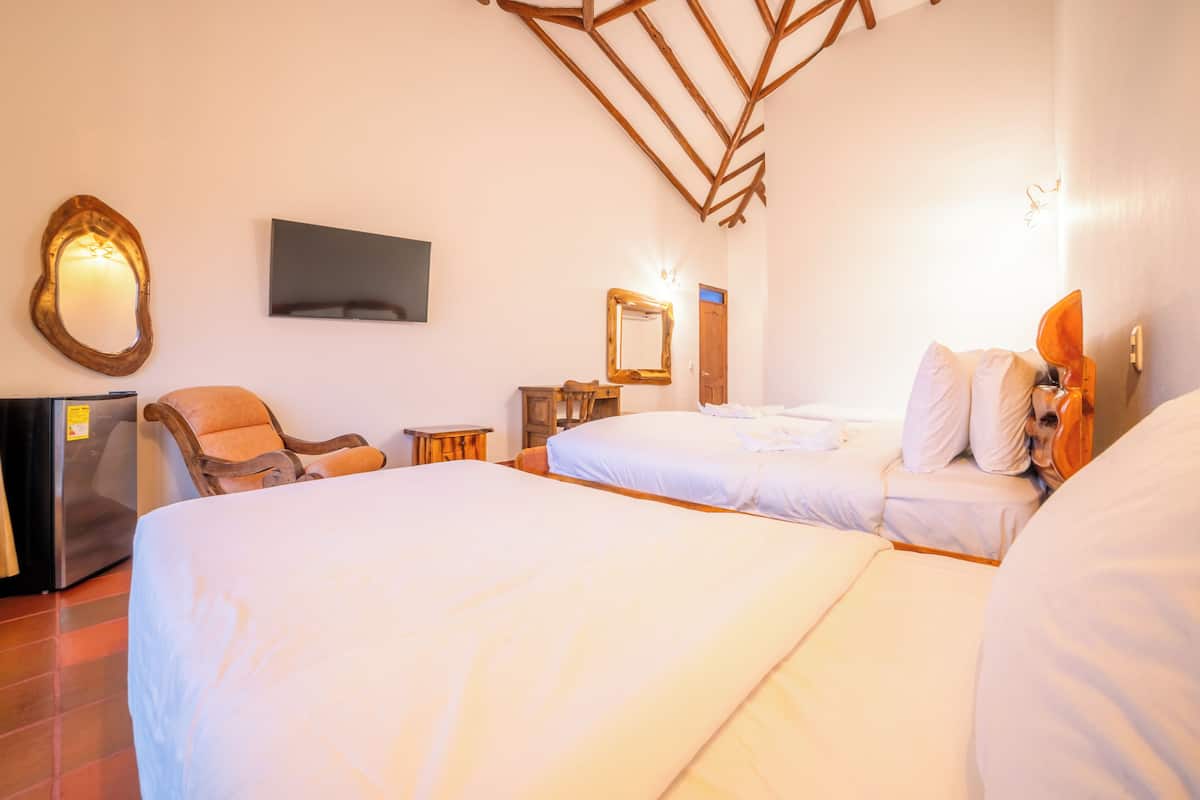 Quarto de hotel com duas camas, televisão, espelho e detalhe no teto em madeira.