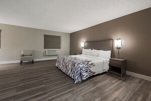 Quarto com cama, mesas de cabeceira, uma cadeira e janela com persianas.