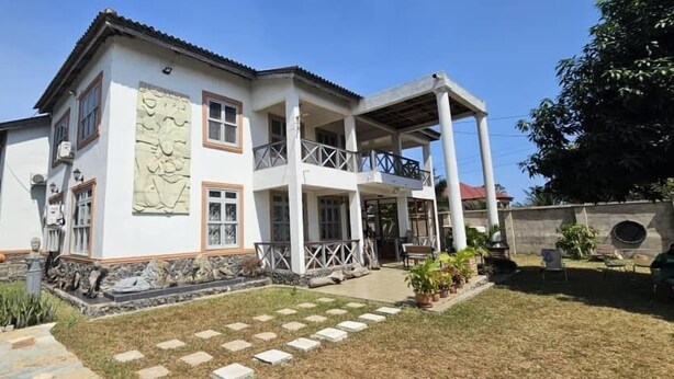 Uma casa de dois andares com varanda, fachada de pedra e gramado bem cuidado.