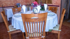 Uma mesa de jantar posta com toalhas brancas, cadeiras de madeira e um vaso com flores.