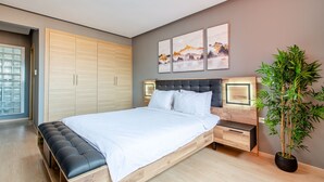 Quarto moderno com uma cama grande, guarda-roupa de madeira, mesas de cabeceira e um vaso com planta.