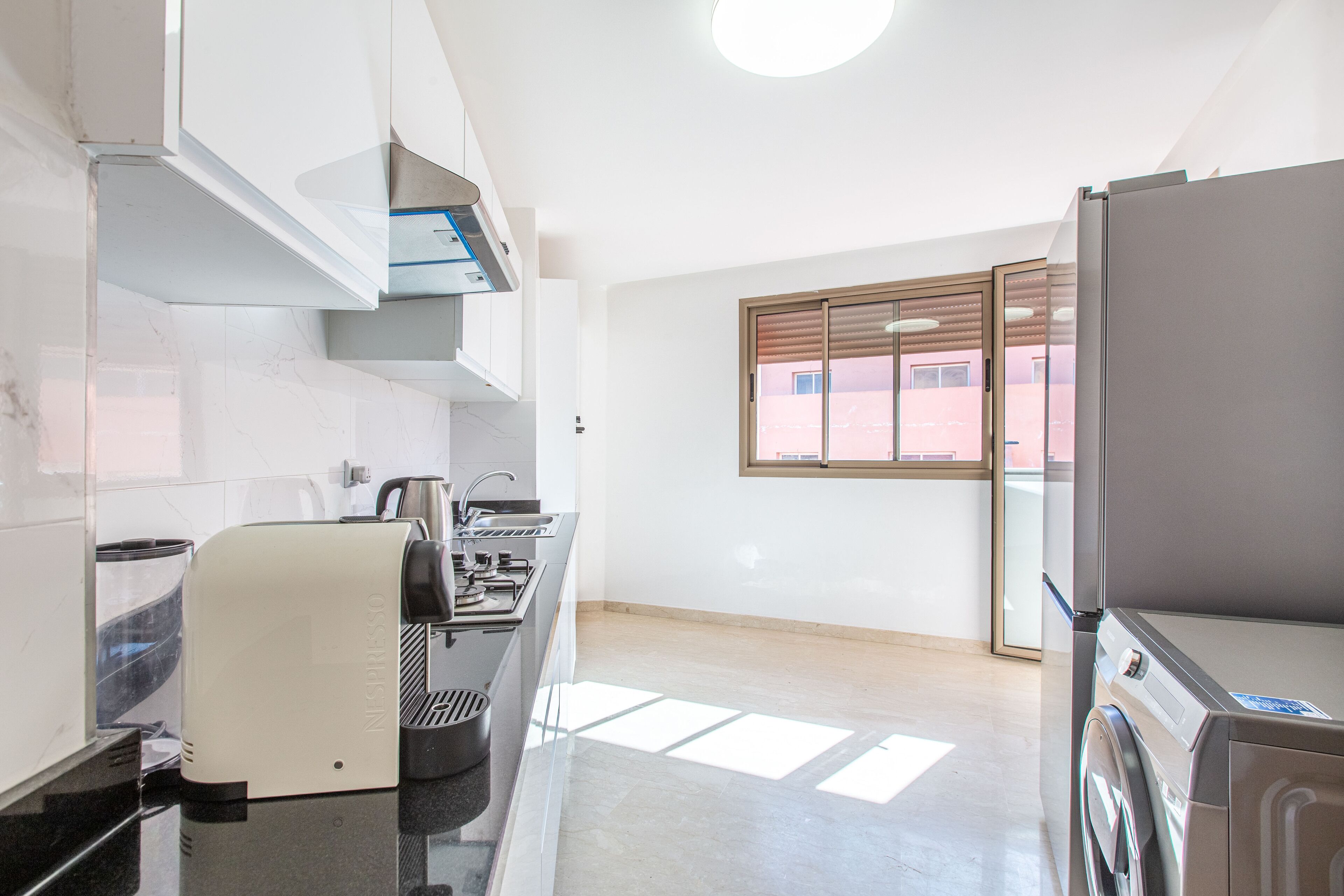 Uma cozinha compacta com cafeteira, máquina de lavar roupa e janela com persianas.