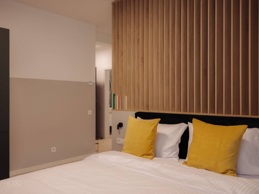 Quarto de hotel moderno com uma cama grande, cabeceira de madeira e paleta de cores neutras.