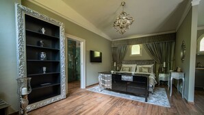 Quarto com um espelho grande e ricamente decorado, cama com cabeceira estofada, candelabro e closet espaçoso com prateleiras.