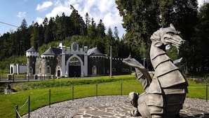 Uma estátua de dragão de pedra em frente a um edifício semelhante a um castelo, com uma placa que diz 'RUDNOVA'.