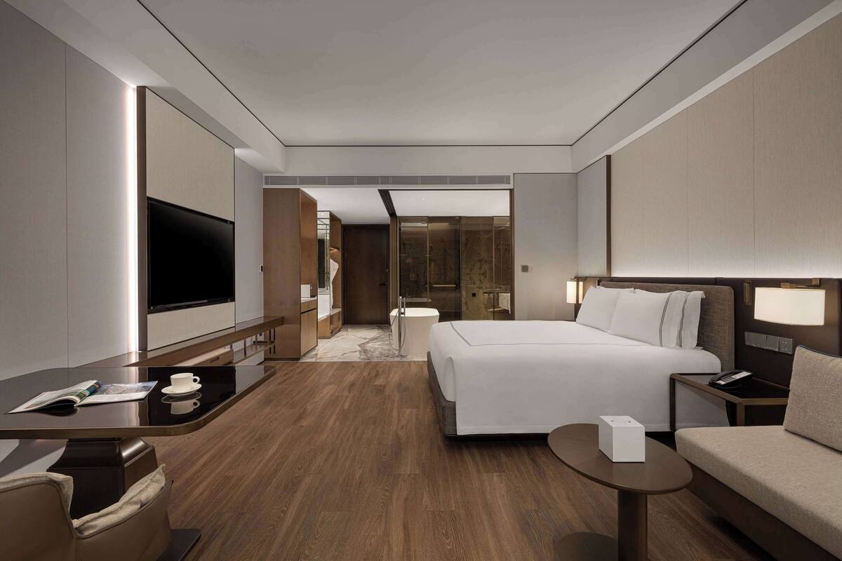 Quarto de hotel moderno com uma cama grande, televisão de tela plana, escrivaninha com cadeira e um sofá.