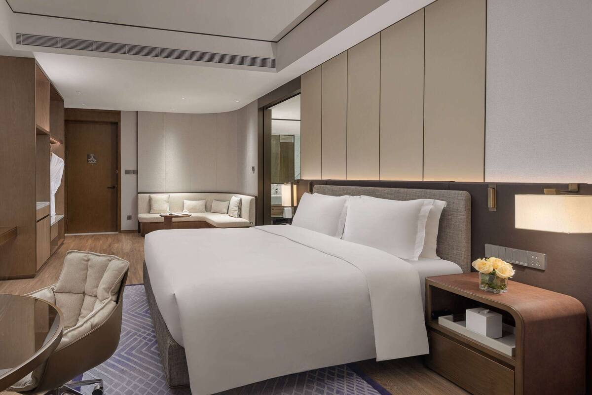 Quarto de hotel moderno com uma cama grande, um espaço de estar, uma escrivaninha e um guarda-roupa.