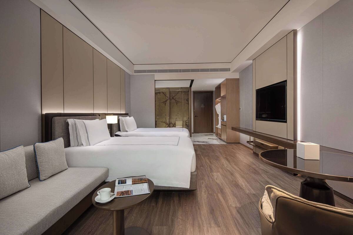 Quarto de hotel moderno com uma cama grande, um sofá, uma mesa pequena e uma televisão.