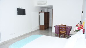 Quarto com uma cama, uma cadeira, um guarda-roupa e uma mesa pequena com um vaso de flores.