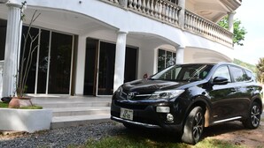 Um SUV preto estacionado em frente a um edifício branco com varanda.