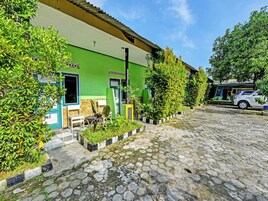 Um edifício verde com um pátio de paralelepípedos, cadeiras brancas e um carro estacionado.
