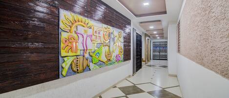 Um corredor com um mural colorido na parede esquerda, piso de azulejos e uma porta no final.