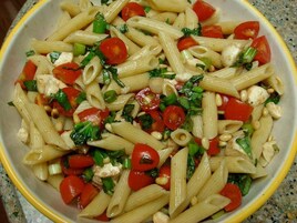 Uma salada de macarrão com penne, tomate e ervas verdes.