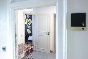 Um corredor com uma porta branca, uma placa com o número 4 e uma mesa com uma revista.
