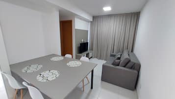 Um espaço de estar moderno com uma mesa de jantar, cadeiras, um sofá e uma televisão.