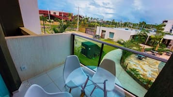 Varanda com duas cadeiras brancas e uma mesa, com vista para área residencial com casas e vegetação.
