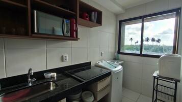 Cozinha com micro-ondas, fogão, pia e janela com vista para palmeiras.