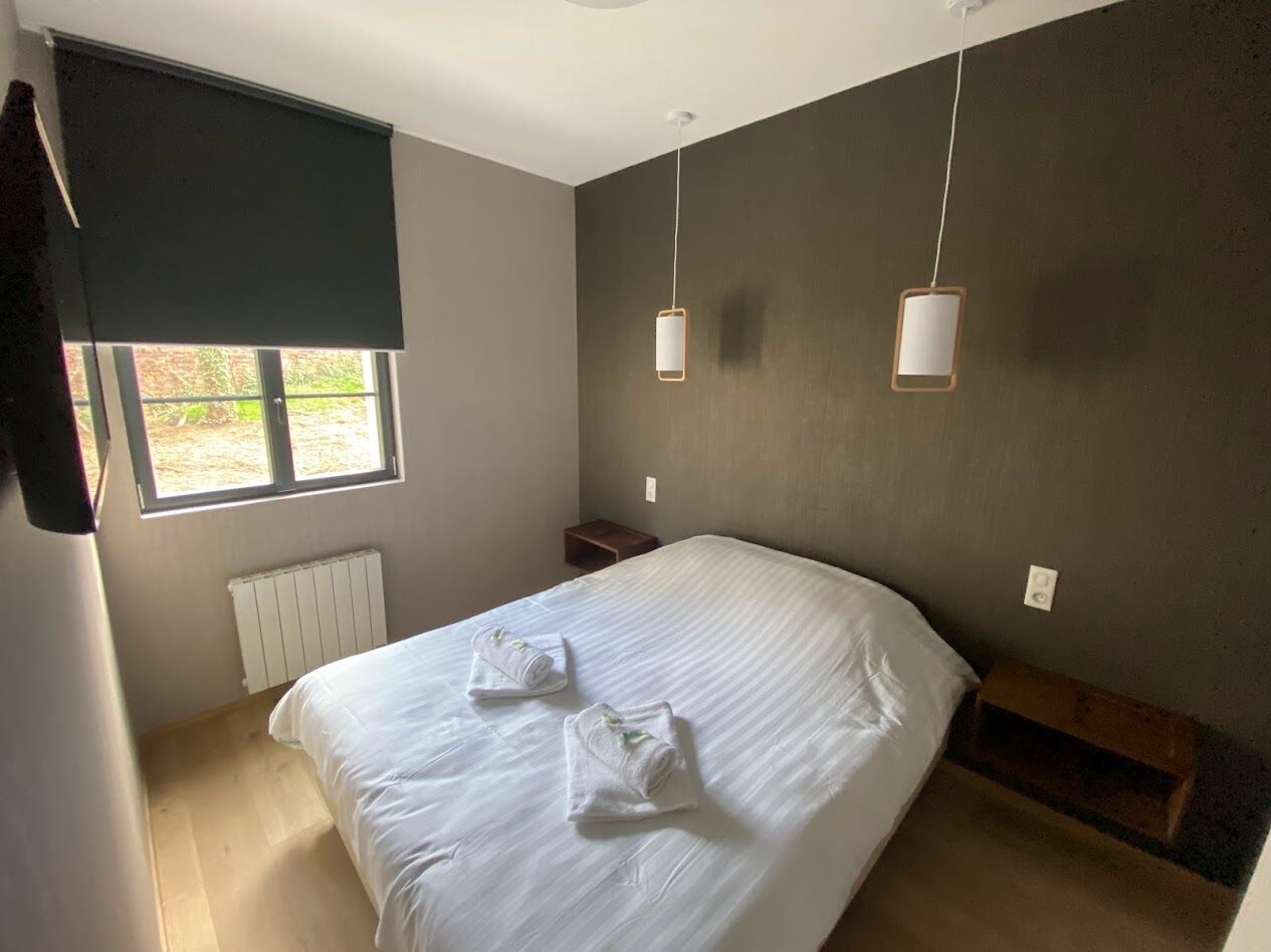 Quarto com uma cama grande, duas mesas de cabeceira, uma janela com cortina e um radiador.