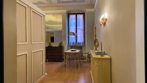 Um corredor com piso de madeira, uma mesa de jantar com cadeiras, um espelho e um abajur.