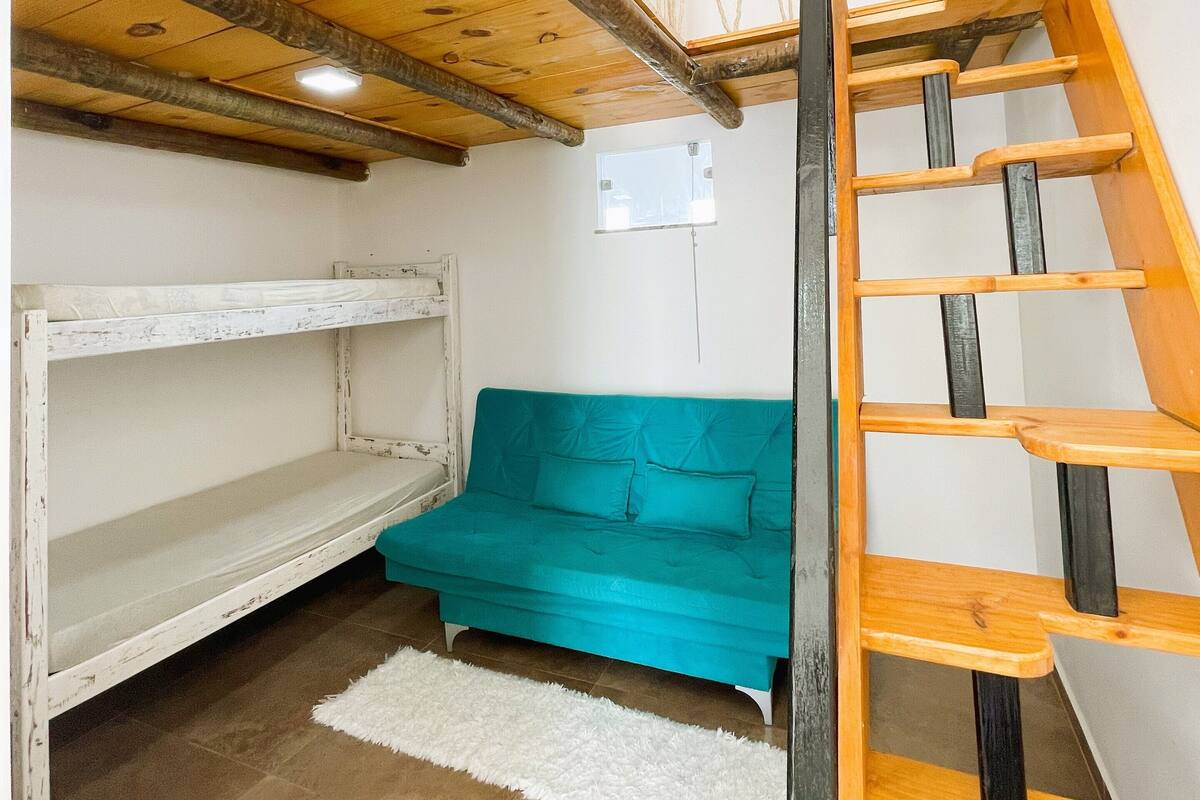 Um quarto com uma cama de solteiro, um sofá verde-água, uma escada de madeira e um tapete branco.